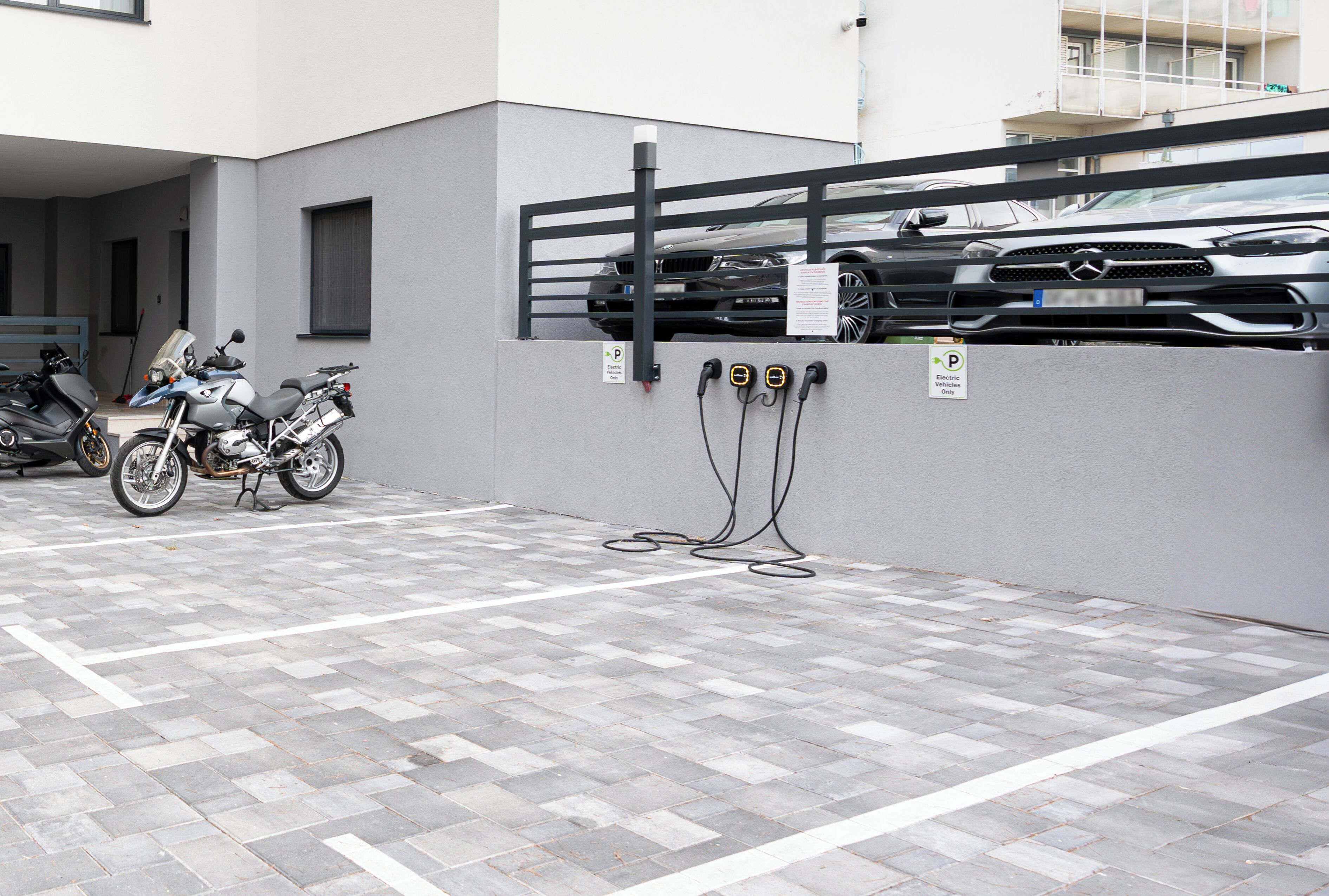 Uma área de estacionamento com estações de carregamento para veículos elétricos, uma moto e um carro.