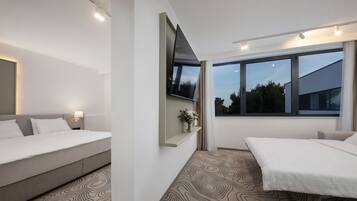 Quarto de hotel moderno com uma cama grande, um sofá-cama menor, uma televisão de tela plana na parede e uma janela com vista para o exterior.