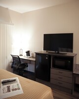 Quarto de hotel com cama, escrivaninha, televisão, frigorífico e micro-ondas.