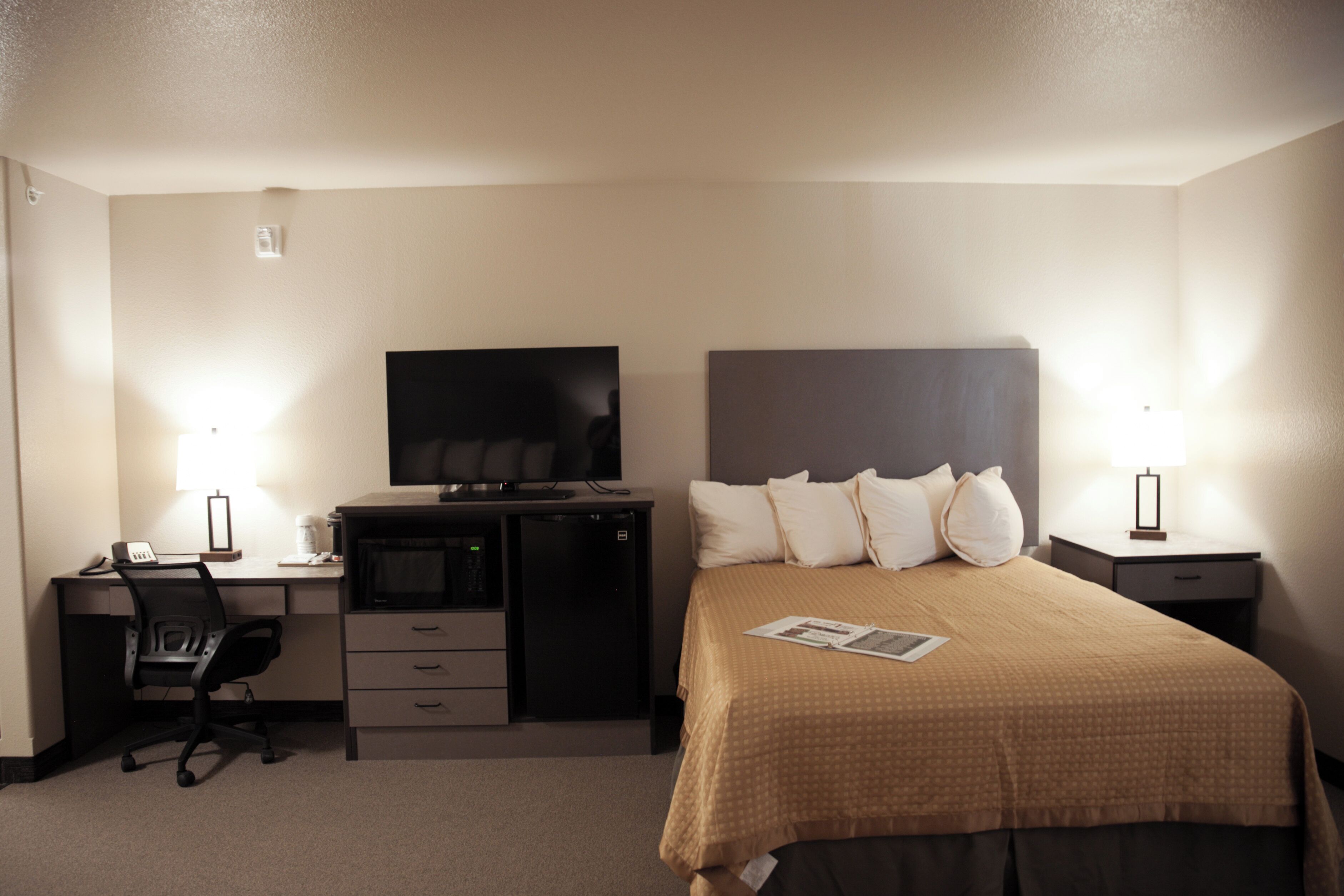 Quarto de hotel com cama, escrivaninha com computador, televisão e micro-ondas.