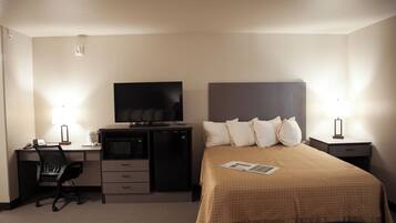 Quarto de hotel com cama, escrivaninha com computador, televisão e micro-ondas.