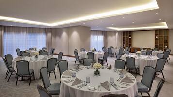 Sala de conferências com mesas redondas, cadeiras cinzas e toalhas de mesa brancas.