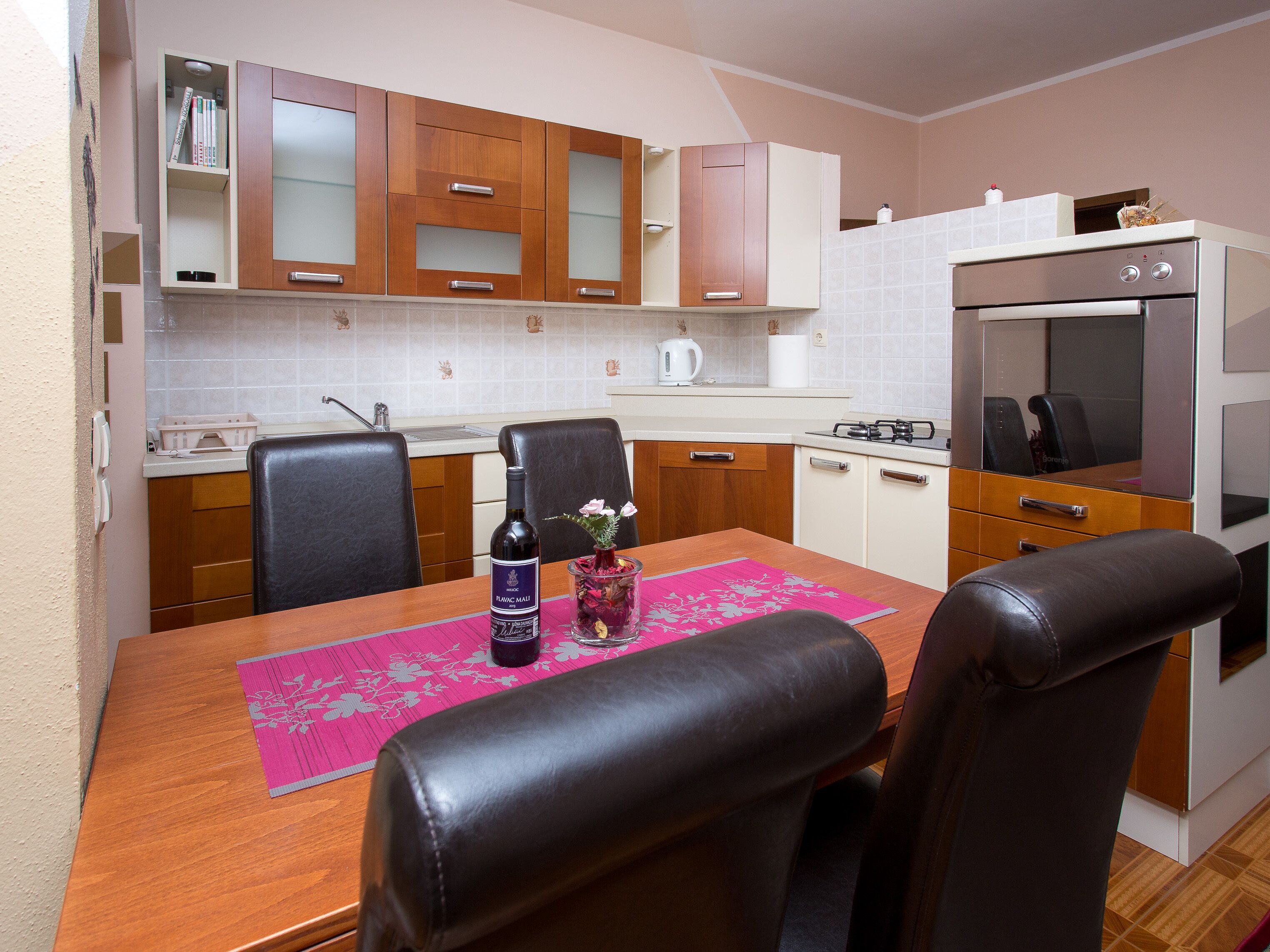 Uma cozinha compacta com armários de madeira, uma mesa de jantar com cadeiras e um forno embutido.