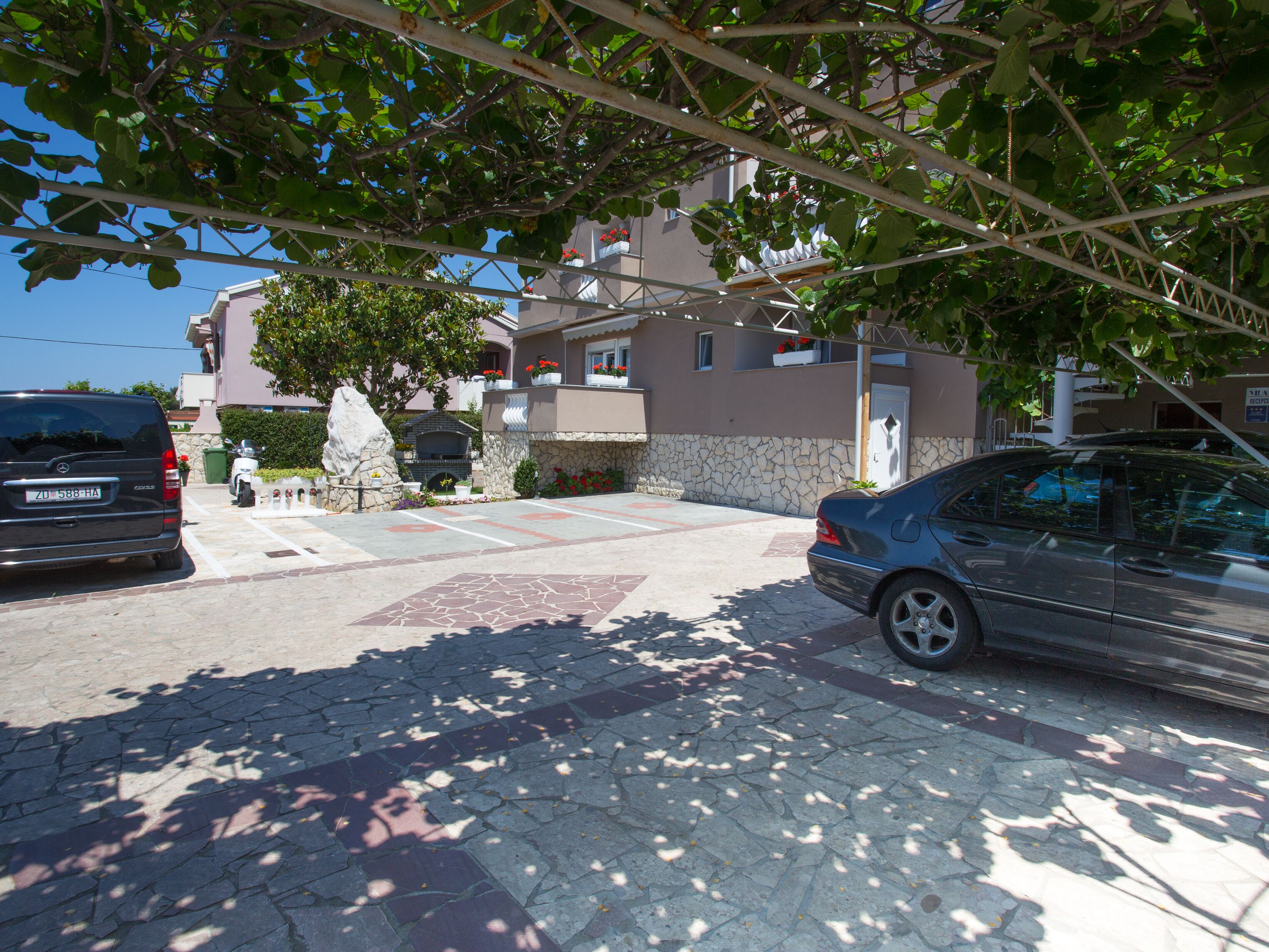 Vista da rua com carros estacionados, um caminho de pedra e um edifício com fachada de pedra e varanda com plantas em vasos.
