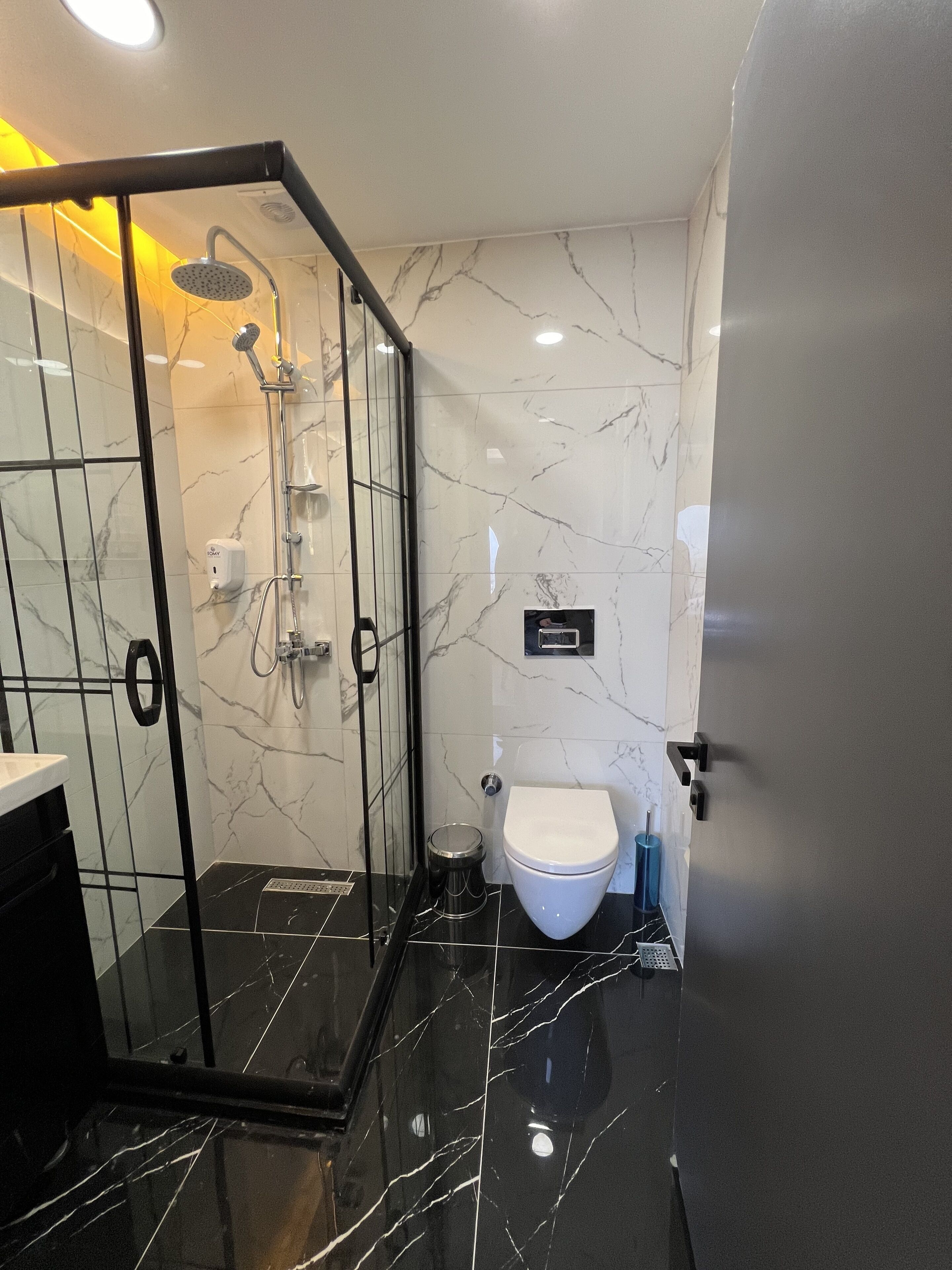 Um banheiro moderno com chuveiro em gabinete de vidro, vaso sanitário e parede revestida de mármore.
