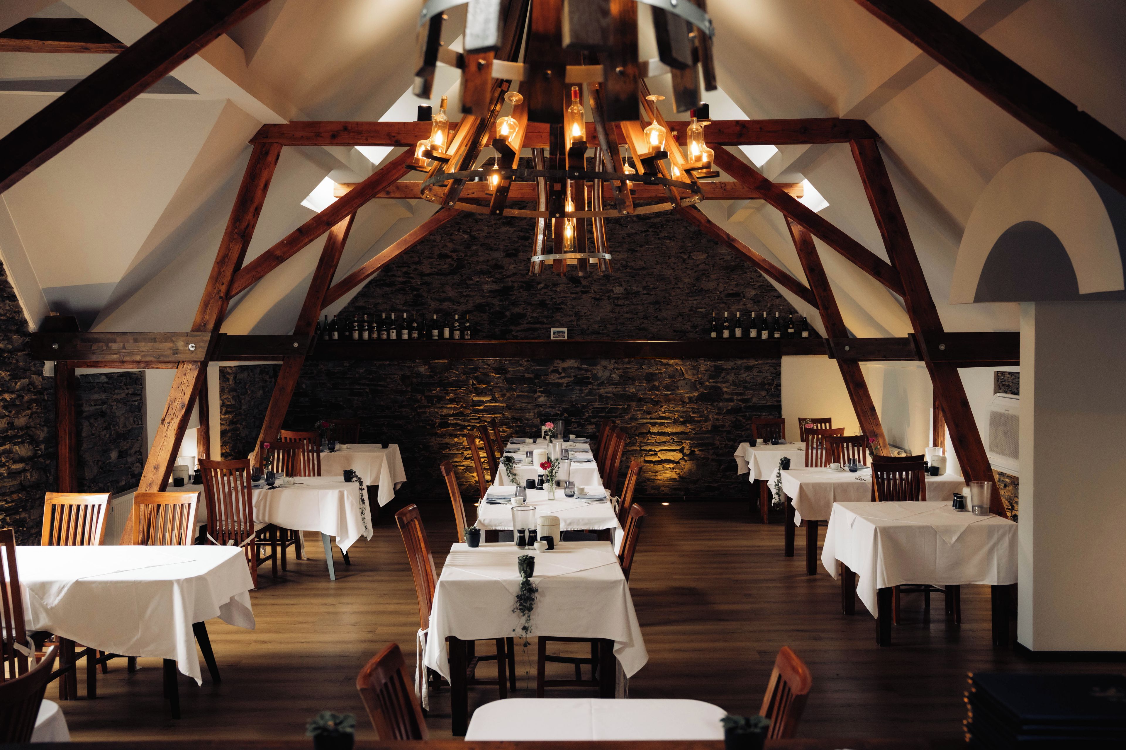 Um restaurante com vigas de madeira altas, paredes de pedra e mesas preparadas para refeições.