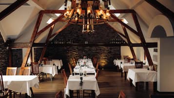 Um restaurante com vigas de madeira altas, paredes de pedra e mesas preparadas para refeições.
