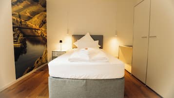 Cama bem arrumada com lençóis brancos em quarto moderno de hotel, com um mural grande na parede, mesa de cabeceira com abajur e guarda-roupa.