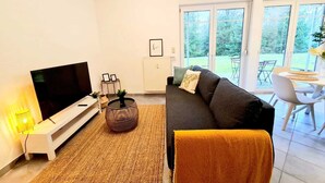 Uma sala de estar com televisão, sofá e área de jantar com mesa e cadeiras.