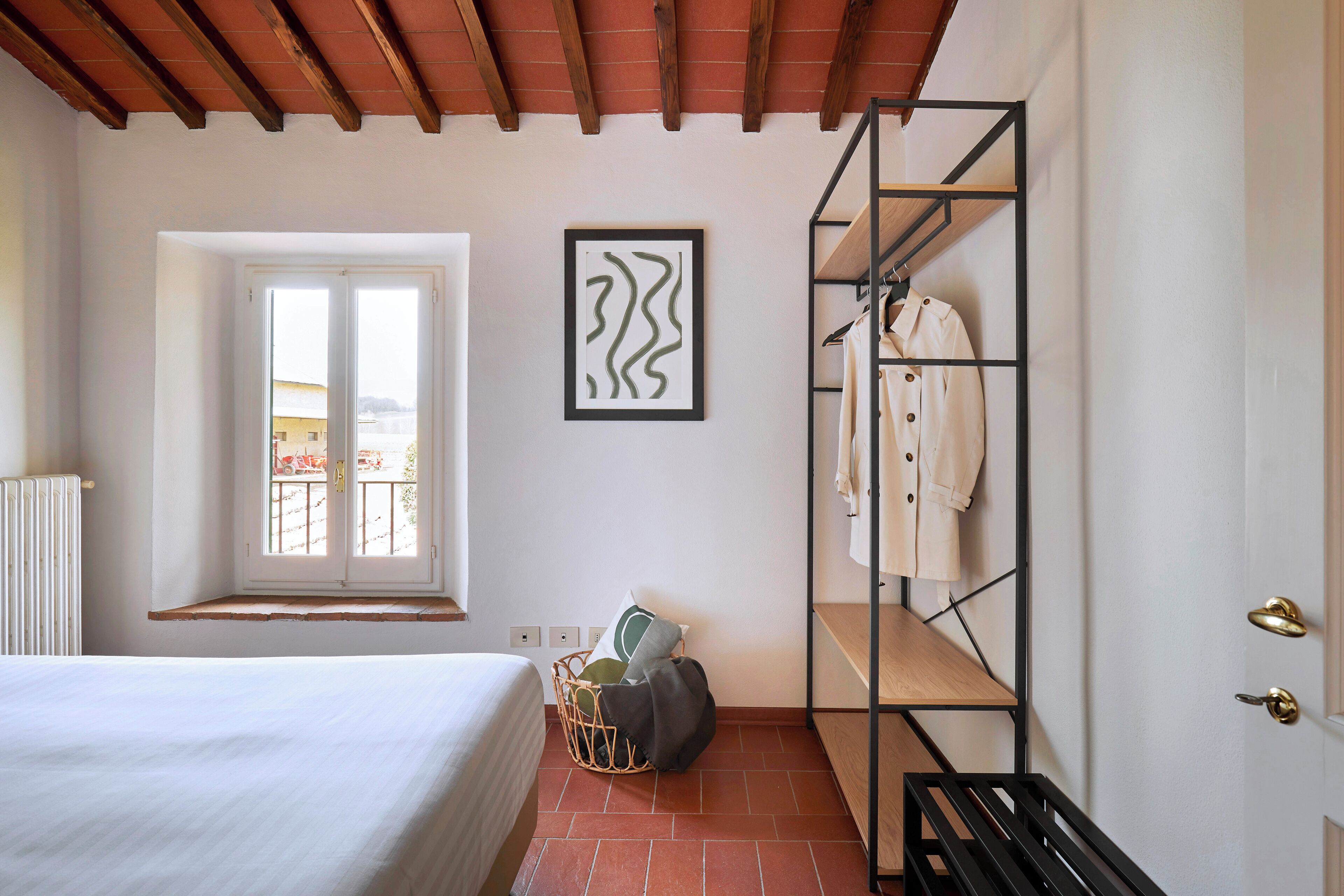 Quarto com cama, janela, radiador, prateleira com roupas e quadro emoldurado.