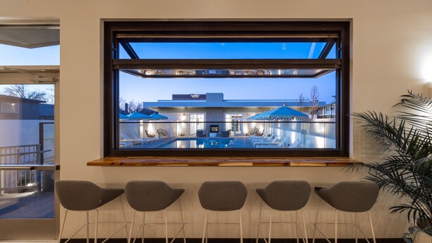Interior moderno com uma grande janela com vista para uma área de piscina, bancada de bar e um edifício com uma placa.