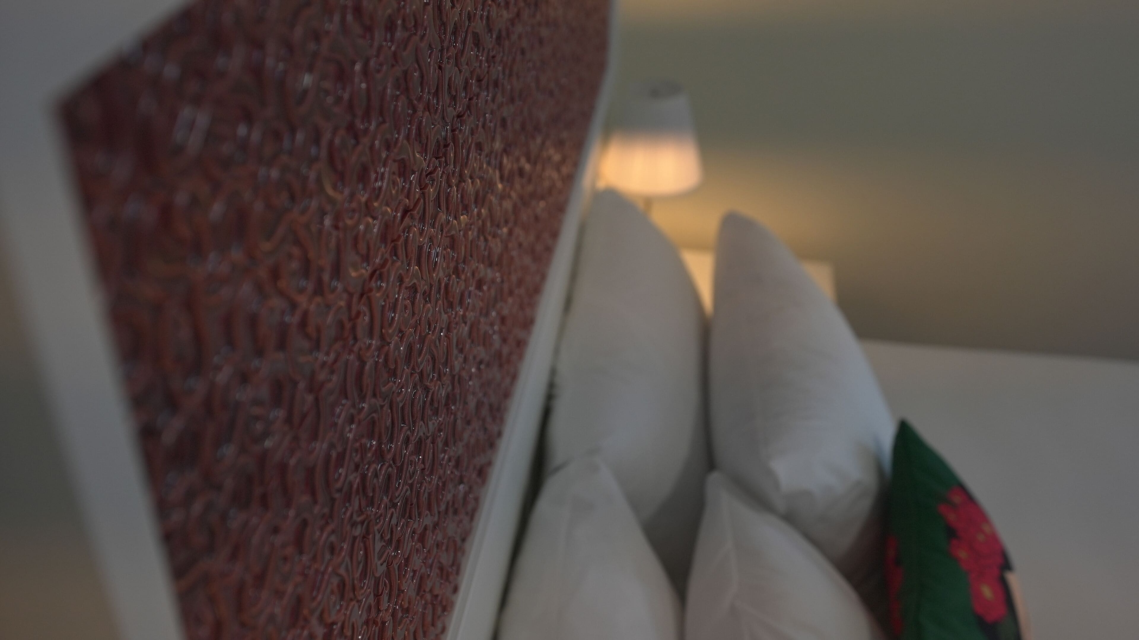 Detalhe de uma parede texturizada e um travesseiro branco com um desenho floral vermelho.