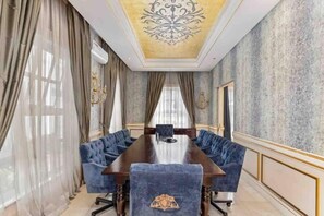 Uma sala de conferências com uma mesa comprida, cadeiras estofadas em azul e teto decorativo.