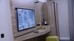 Quarto moderno com televisão integrada numa parede de madeira, uma pequena secretária com comando remoto e um banquinho amarelo.