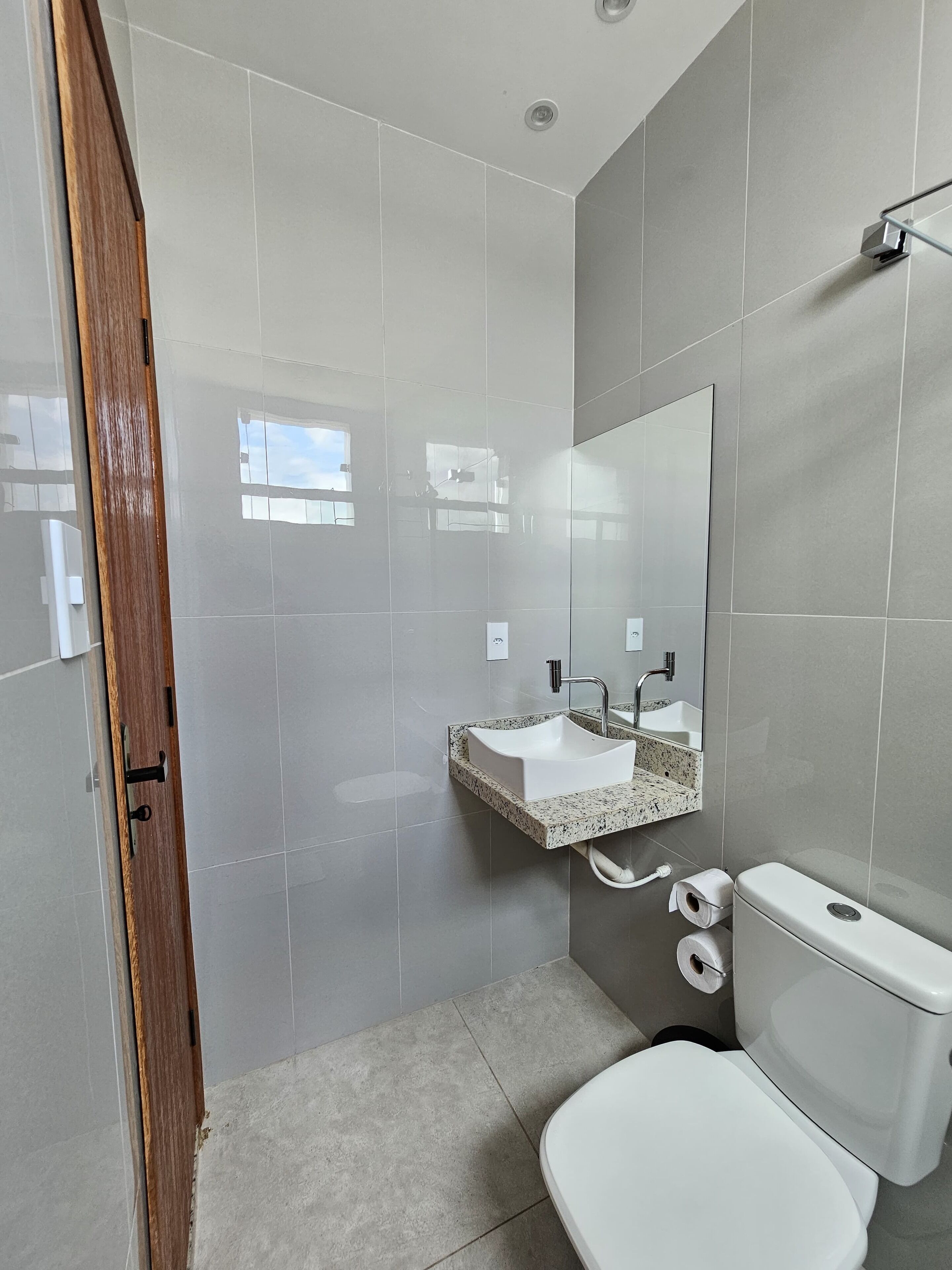 Casa de banho moderna com lavatório branco, espelho e sanita.