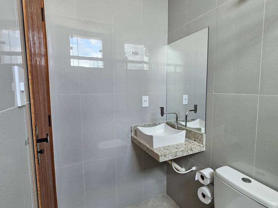 Casa de banho moderna com lavatório branco, espelho e sanita.