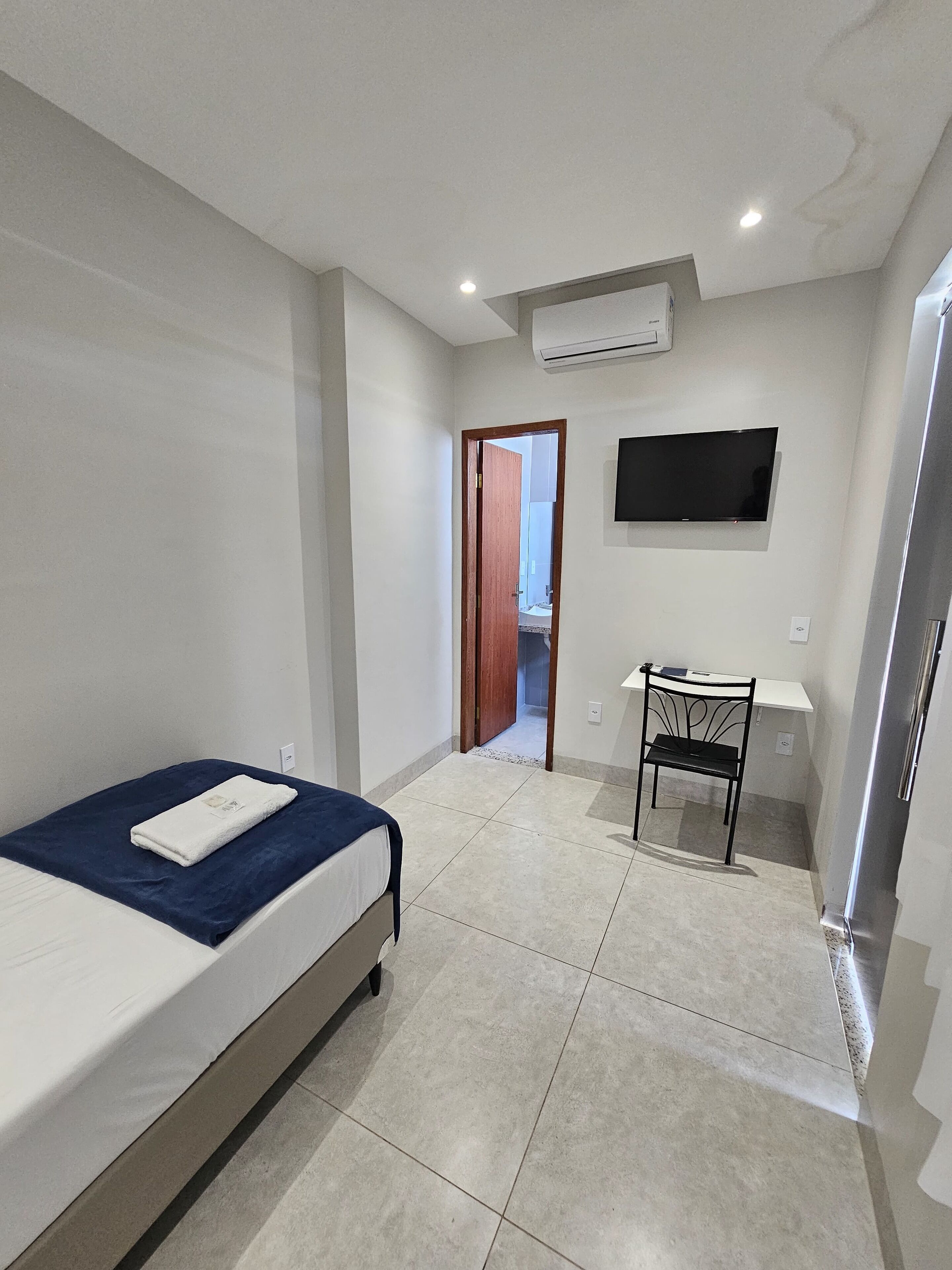 Quarto com cama, escrivaninha, cadeira e televisão.