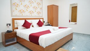 Uma cama bem arrumada com roupa de cama vermelha e branca, uma mesa de cabeceira de madeira com um telefone, um guarda-roupa e um quadro na parede.