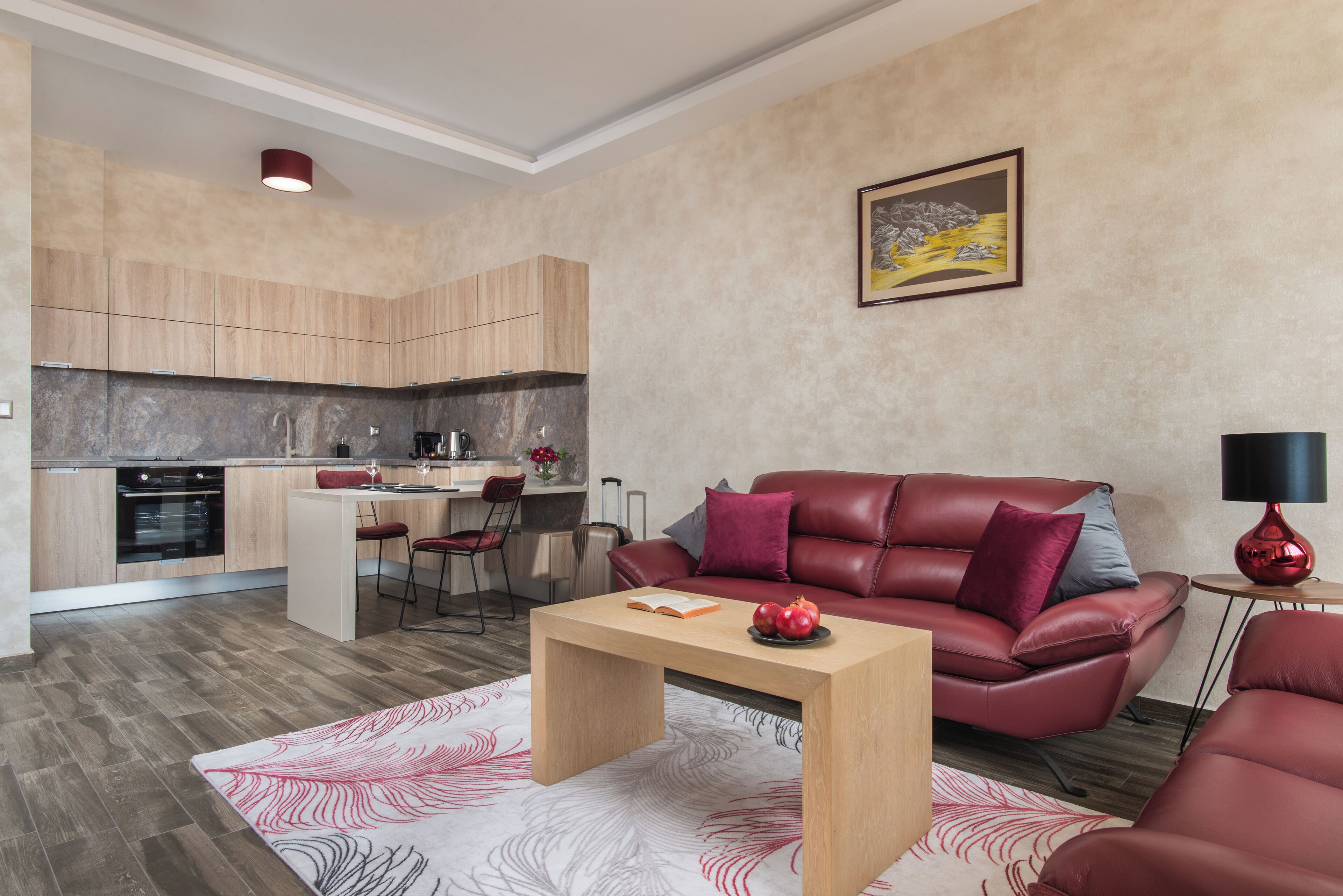 Uma sala de estar moderna com um sofá de couro vermelho, uma mesa de centro de madeira e uma cozinha ao fundo.