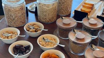 Uma mesa de buffet com diversos alimentos e recipientes, incluindo tigelas com nozes, frutas secas e cereais.