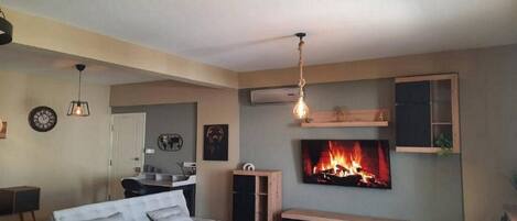 Uma sala de estar moderna com um sofá cinzento, uma televisão fixada na parede e uma lareira.