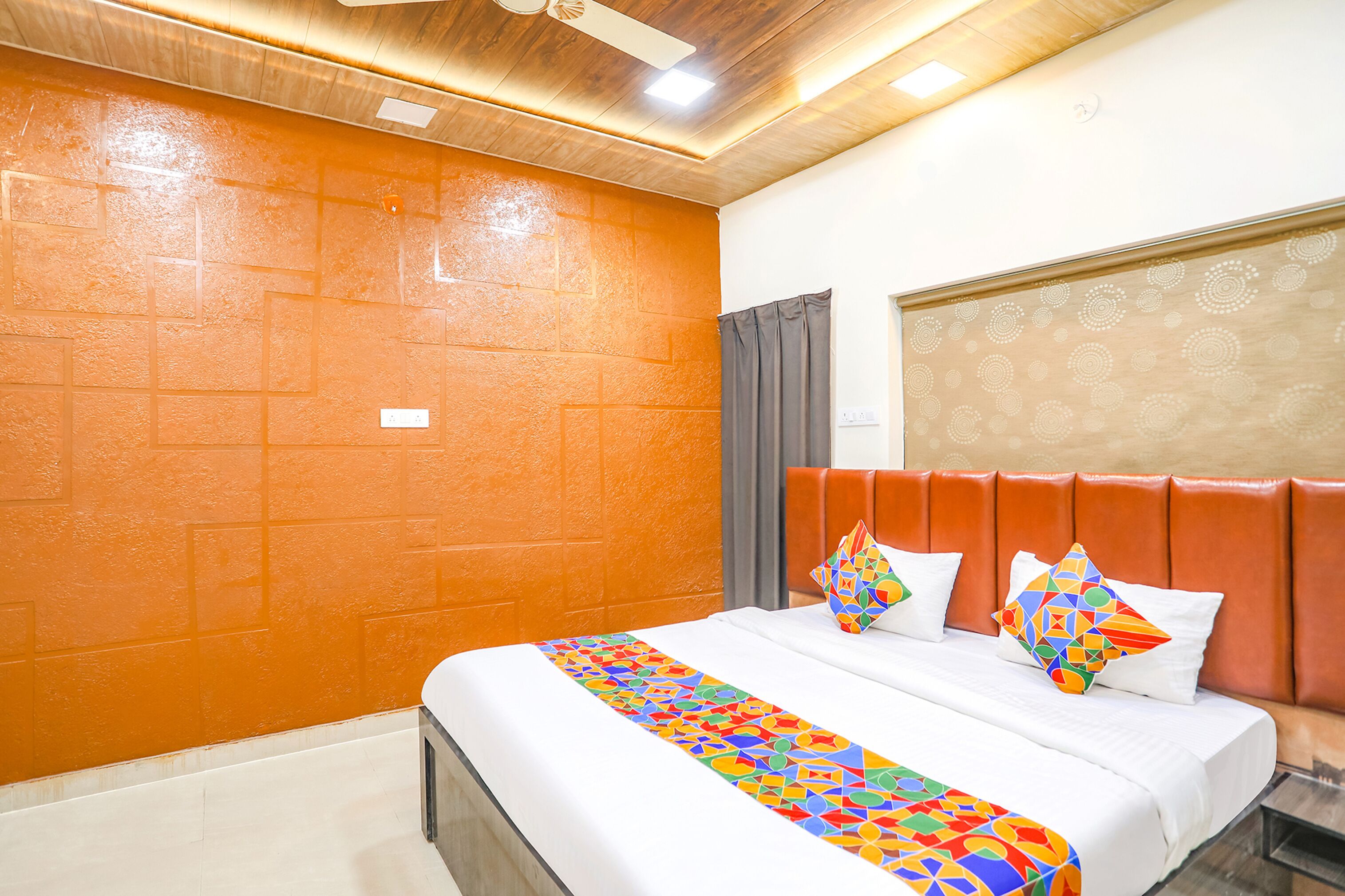 Quarto de hotel com uma cama grande, paredes texturizadas em laranja e um design de teto moderno.