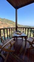 Um deck de madeira com uma mesa posta para dois, com vista para uma paisagem montanhosa.