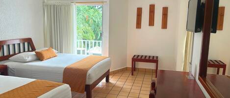 Quarto de hotel com duas camas, cabeceira de madeira, uma mesa pequena, televisão e varanda com cortinas.