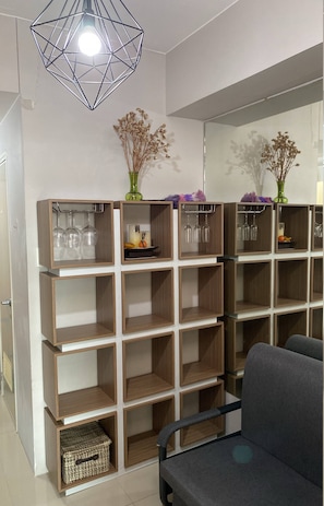 Quarto moderno com sofá cinza, estante de madeira com copos de vinho e luminária pendente geométrica.