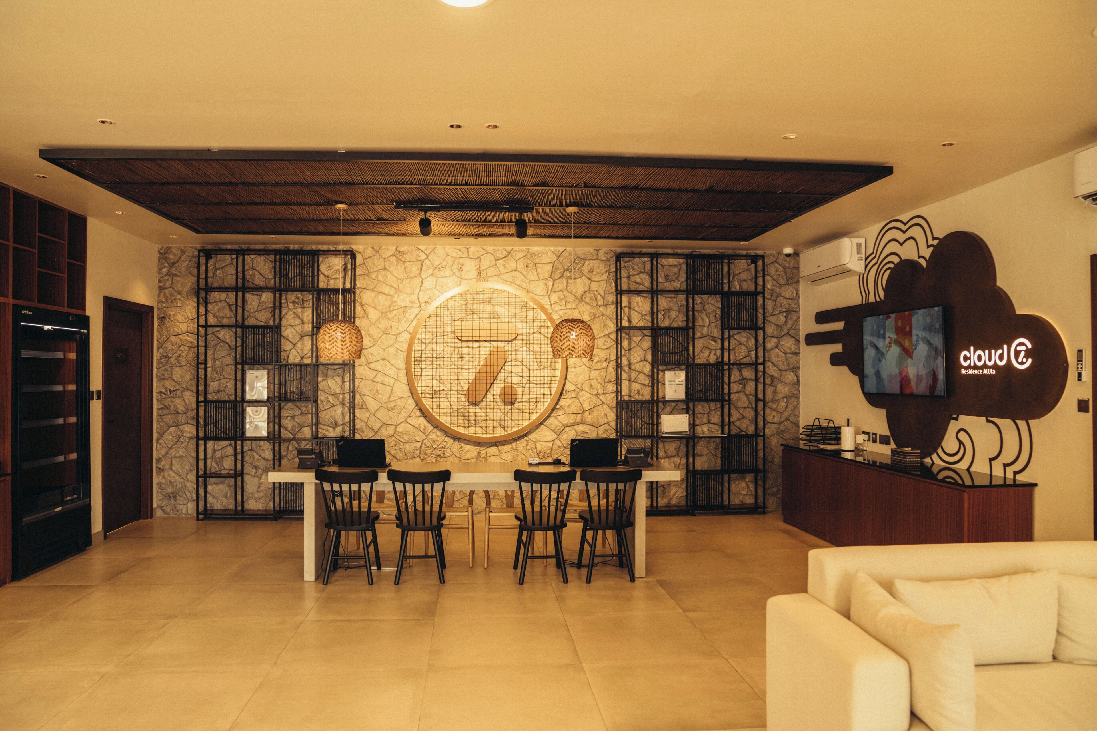 Uma sala de estar moderna com parede de pedra, um relógio redondo, uma televisão e um sofá branco.