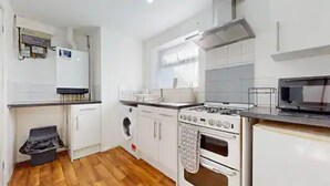 Uma cozinha compacta com eletrodomésticos brancos, máquina de lavar e micro-ondas.
