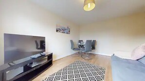 Uma sala de estar moderna com uma televisão de tela plana, um sofá, um tapete estampado e uma área de jantar com cadeiras e uma mesa.