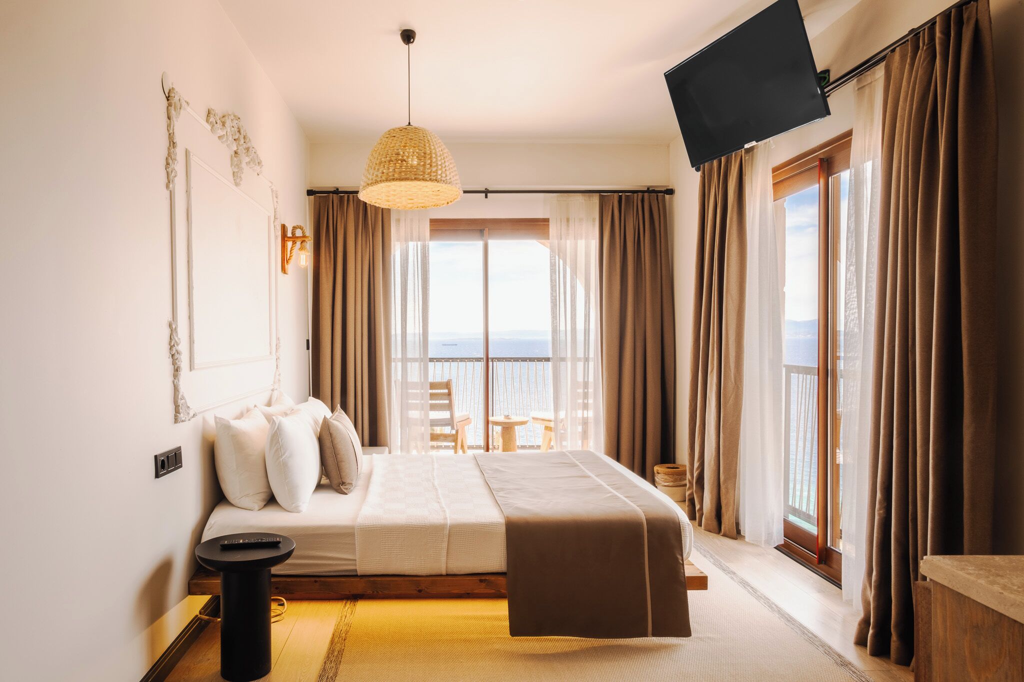 Quarto com cama, televisão, varanda e vista para o mar.
