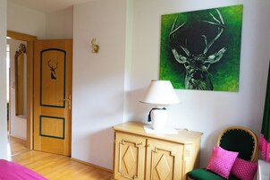 Quarto com porta de madeira, quadro com moldura verde, luminária branca e cadeira verde com almofadas cor-de-rosa.