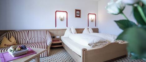 Quarto de hotel com sofá listrado, cama com roupa de cama branca, mesa pequena com cesta de frutas e duas luminárias fixadas na parede.
