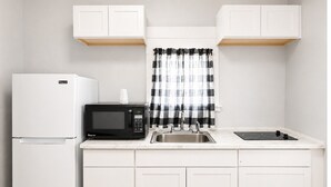Uma cozinha compacta com geladeira, micro-ondas, pia e um fogão por indução preto.