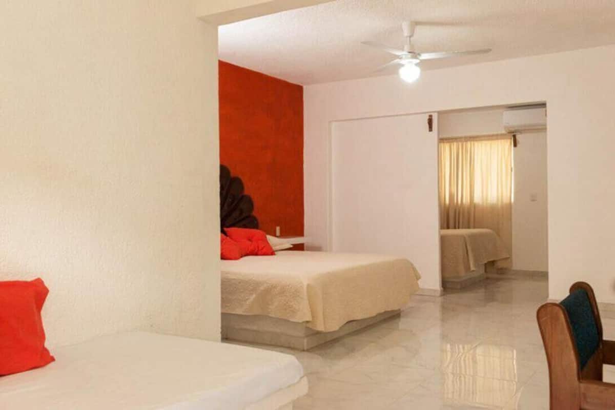 Quarto de hotel com duas camas, ventoinha no teto e banheiro com chuveiro.