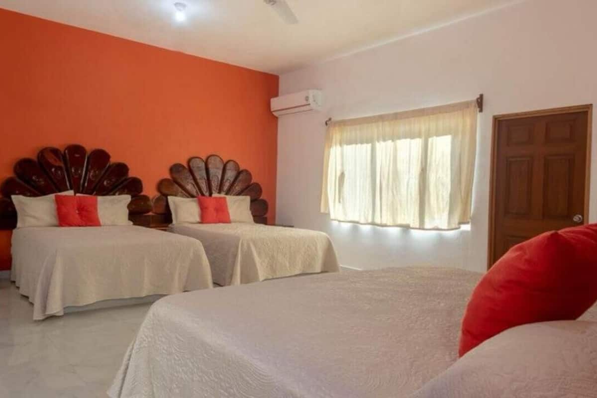 Quarto de hotel com duas camas, uma janela com cortinas, um aparelho de ar condicionado e uma porta de madeira.