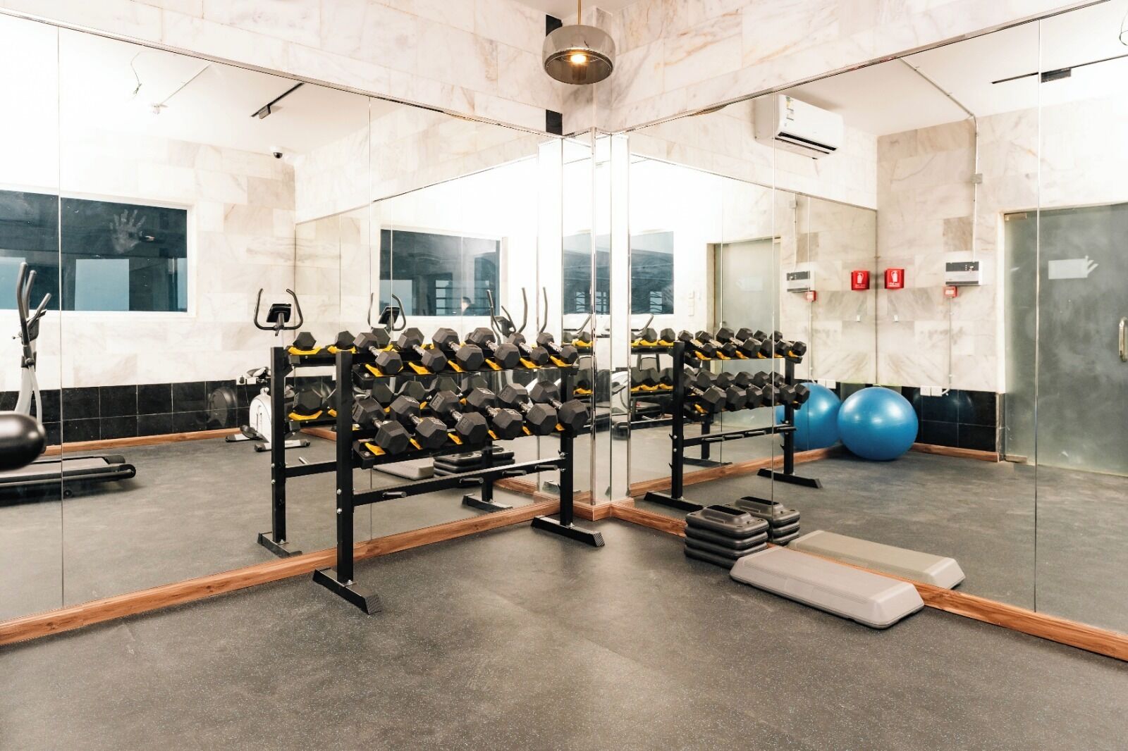 Uma academia com espelhos, suportes para pesos, halteres, esteira e bolas de exercício.