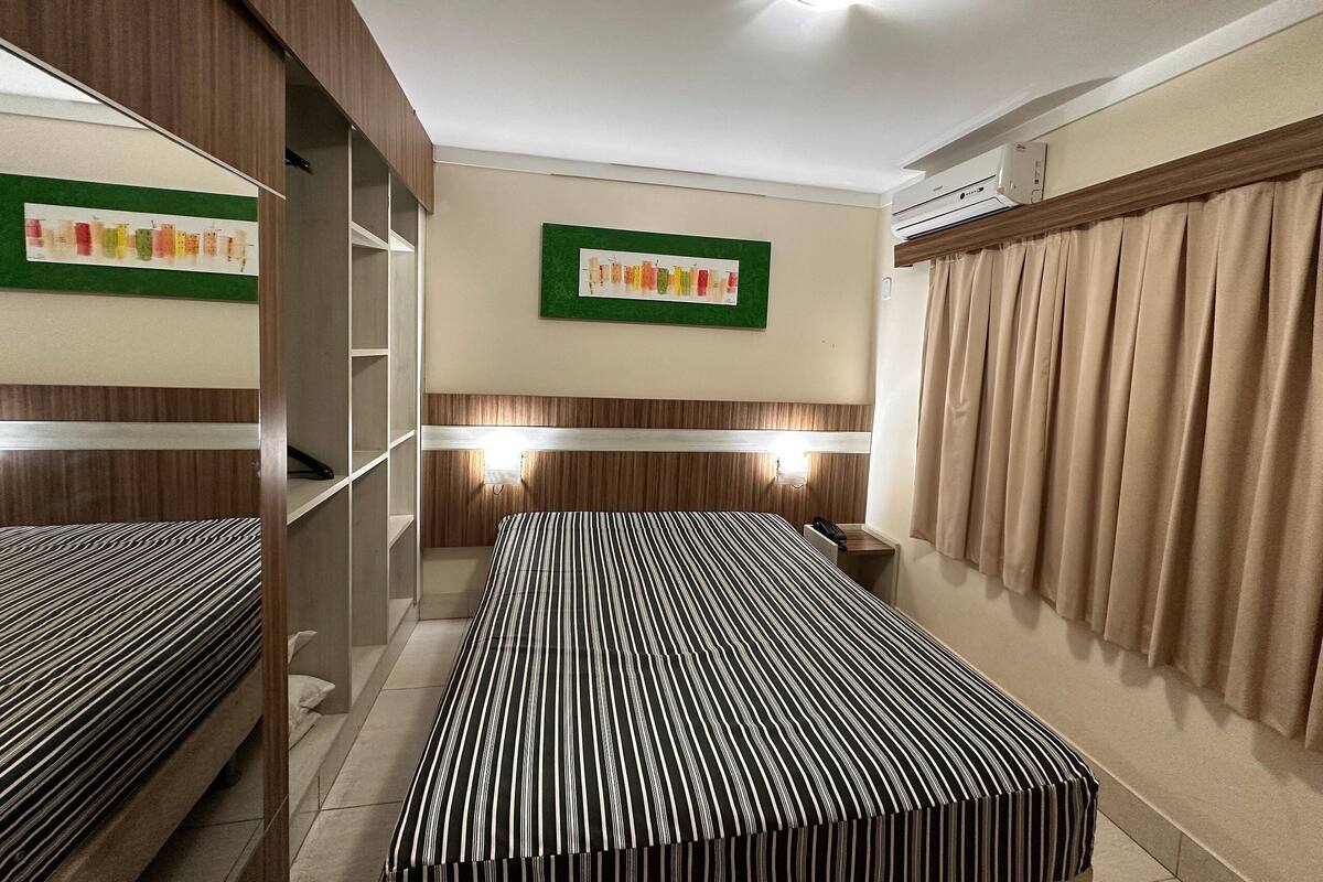 Quarto de hotel com beliches, um quadro com moldura verde, ar-condicionado fixado na parede e cortina.