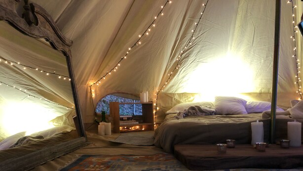 Um quarto tipo tenda aconchegante, com cama, mesa de cabeceira, velas e luzes de cordão.