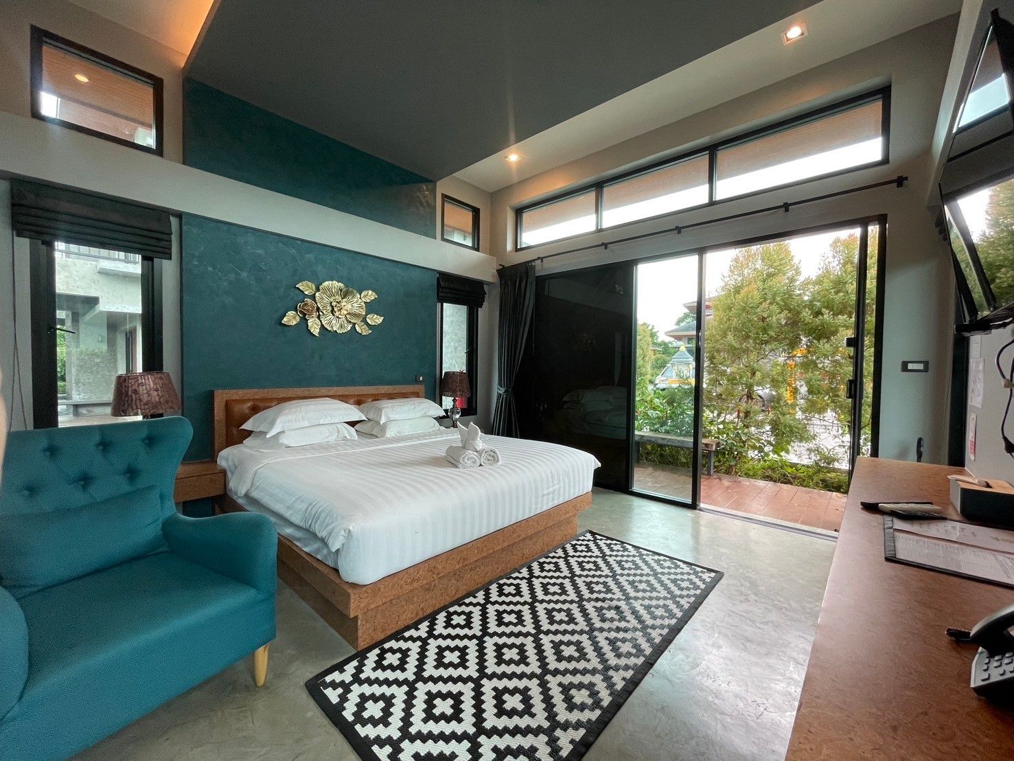 Quarto moderno com uma cama grande, uma poltrona azul, um tapete estampado e uma escrivaninha com telefone.
