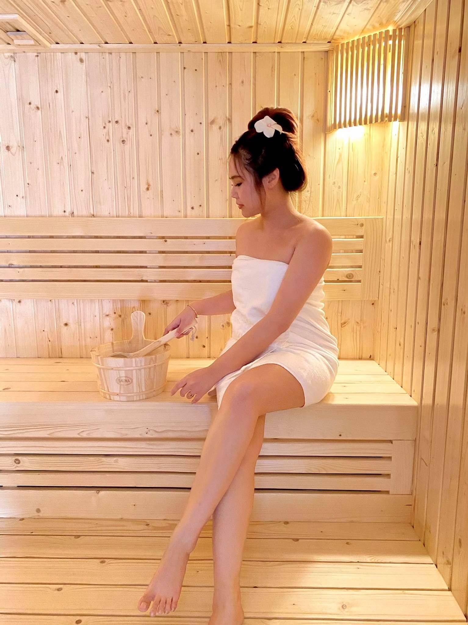 Uma pessoa sentada em uma sauna de madeira com um balde.