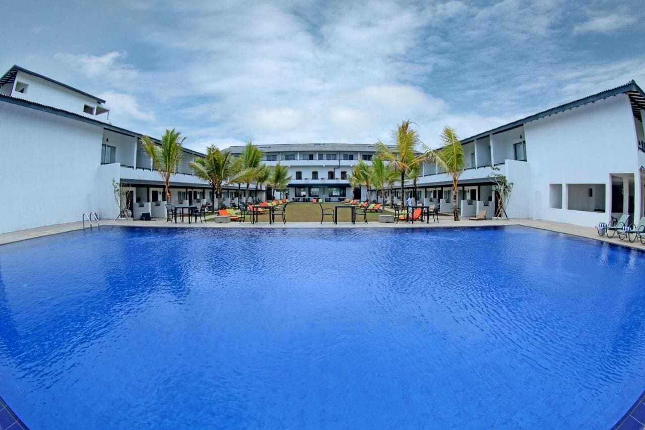 Piscina com espreguiçadeiras e palmeiras, cercada por um edifício com várias varandas.