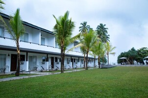 Um hotel com fachada branca, vários quartos e um pátio gramado com palmeiras.