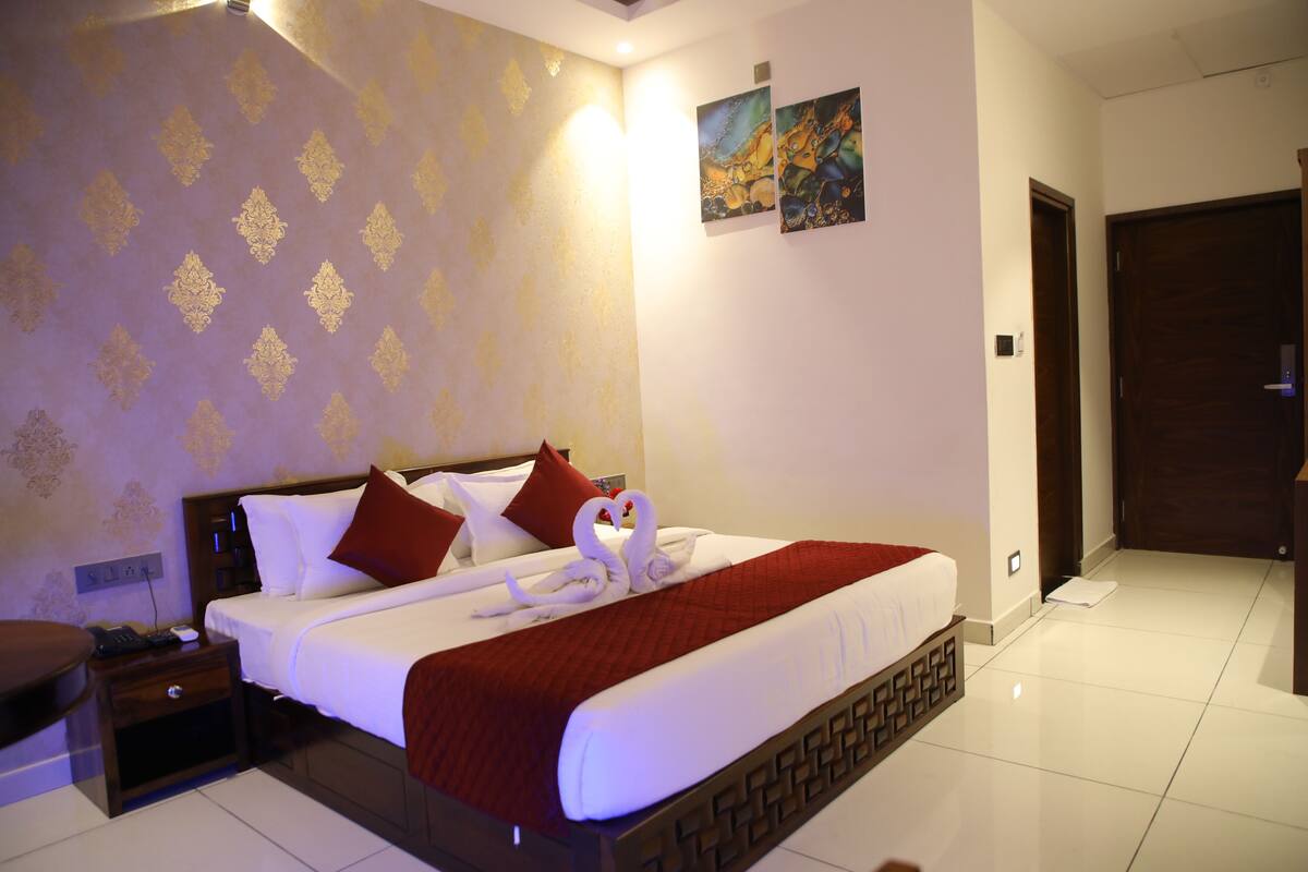 Quarto de hotel com uma cama bem arrumada, mesa de cabeceira com abajur e um quadro na parede.