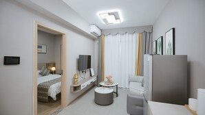 Quarto de hotel moderno com cama, mesa de cabeceira, televisão e uma pequena área de estar com poltrona e apoio para os pés.