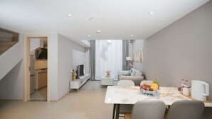 Cozinha moderna com forno embutido e micro-ondas, sala de jantar com mesa e cadeiras de mármore, e sala de estar com sofá e televisão.