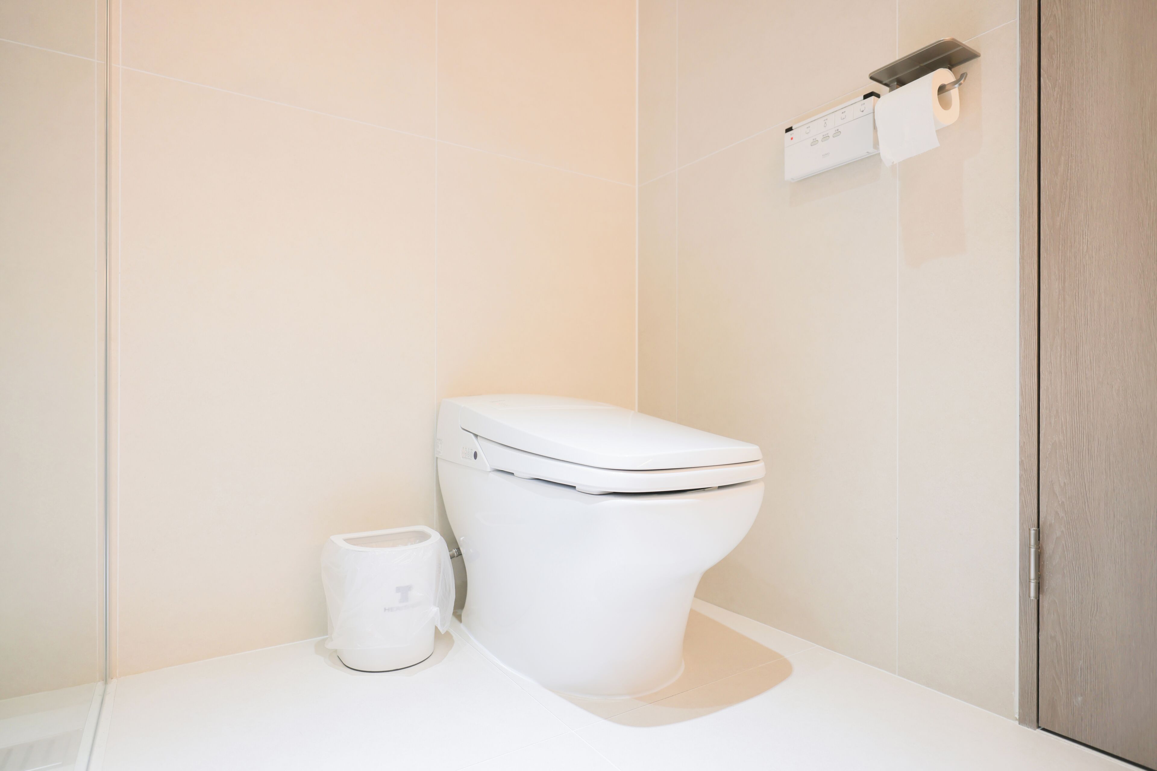 Um banheiro moderno com vaso sanitário branco, suporte para papel higiênico e uma pequena lixeira.