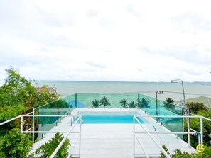 Piscina com barreira de vidro, rodeada por vegetação e com vista para um corpo de água.